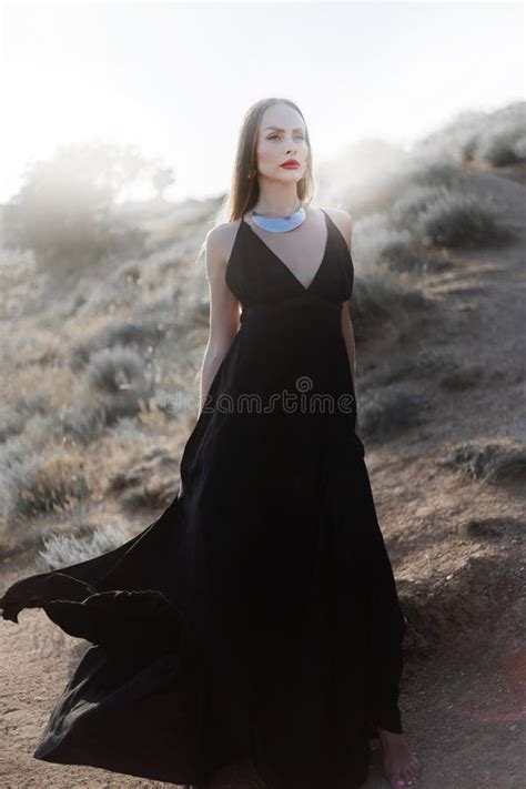 Woman In Black Dress Stands Looking Into The Sea On A Rock Stock Image