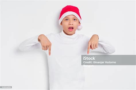 크리스마스 모자를 쓴 놀란 아시아 남자의 초상화가 손가락을 가리키며 사람들이 흰색 배경에 고립되어 따르도록 초대합니다 12 13세에 대한 스톡 사진 및 기타 이미지 Istock