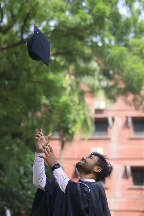 A Man In Black Graduation Gown Throwing The Black Graduation Cap · Free
