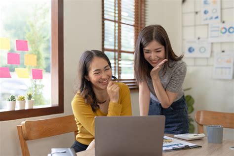 직장에서 행복을 표현하는 두 명의 아시아 사업가가 현대 사무실에서 노트북 컴퓨터로 미소를 짓고 기쁨으로 손을 든다 20 24세에