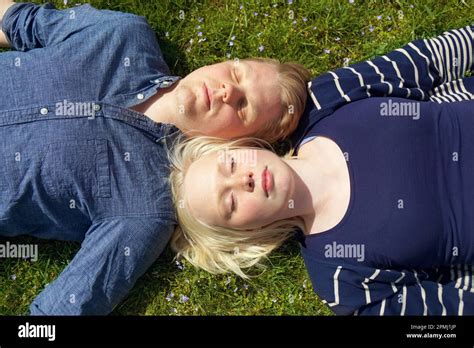 Young Couple Laying On Grass With Eyes Closed And Their Heads Side By