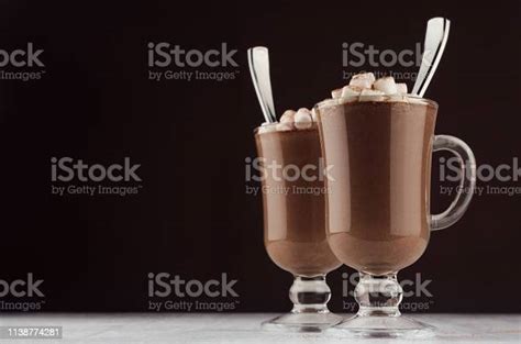 우아한 핫 초콜릿 두 클래식 아일랜드어 커피 유리에 마 시 멜로와 어두운 갈색 벽과 흰색 나무 테이블에 실버 숟가락 복사 공간