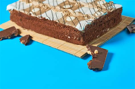 견과류가있는 깨진 초콜릿 바 근처의 대나무 매트에 체크 무늬 직사각형 케이크 한 개가 파티의 파란색 테이블에 놓여 있습니다 축