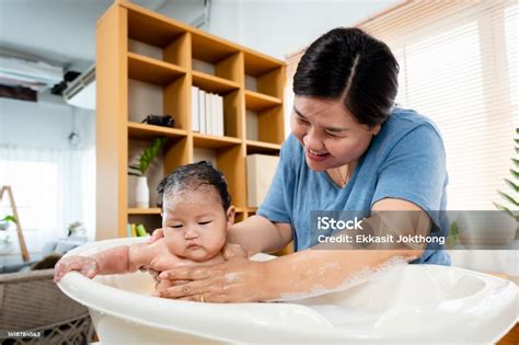 싱글맘의 아시아 손이 손을 뻗어 갓 태어난 딸을 목욕시키기 위해 소녀의 몸보다 큰 욕조 비누 거품으로 가득 찬 소녀의 머리와
