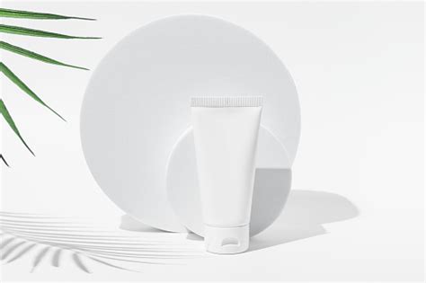 하얀 화장품 크림 튜브는 야자수 잎이 있는 하얀 바탕에 하얀 둥근 연단에 있다 자외선 차단 로션 모형 상표가 없는 Spf 크림 0명에 대한 스톡 사진 및 기타 이미지