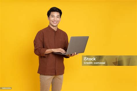 黄色い背景にノートパソコンを持ち立つアジアのビジネスマン 男性のストックフォトや画像を多数ご用意 男性 ノートパソコン アジア