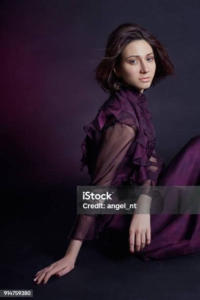 큰 파란 눈을 가진 대비 패션 아르메니아 여자 초상화 보라색 드레스에 어두운 배경에 앉아 사랑 스러운 화려한 여자 이브닝 드레스에 포즈입니다 밝은 메이크업 여자 손에 대한