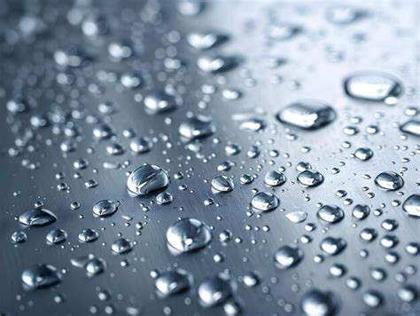 Closeup of water droplets on a smooth metallic surface reflecting light in a softly lit ...