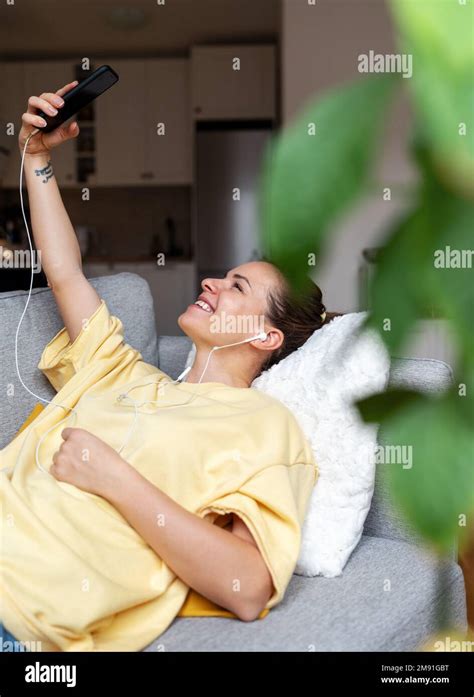 Young Brunette Woman Lying Down On Sofa Living Room And Taking Selfie