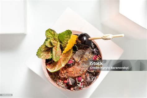 구리 스탠드의 구리 유리에 과일 딸기 및 작은 얼음을 곁들인 여러 종류의 럼에 티키 칵테일 칵테일은 흰색 바탕에 석고 인물 중 석고 인물 위에 서 있습니다 칵테일에 대한