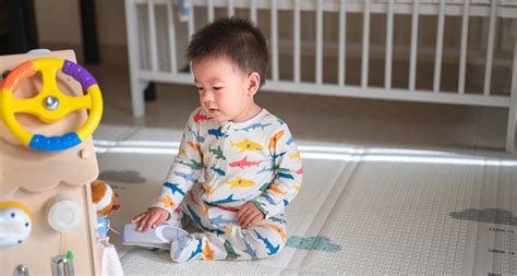 집에서 바닥에있는 아기 금고 부드러운 놀이 매트에 앉아있는 동안 침실에서 큰 활동 상자를 가지고 노는 아기 소년 집에서 노는