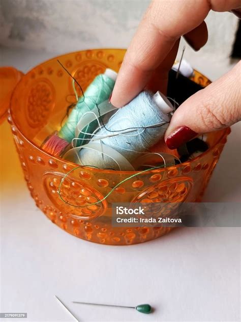 한 여자의 손이 실과 바늘이 들어 있는 상자에서 푸른 실 한 가닥을 꺼냅니다 재봉 및 의류 수리 개념 배경 텍스트를 위한 공간