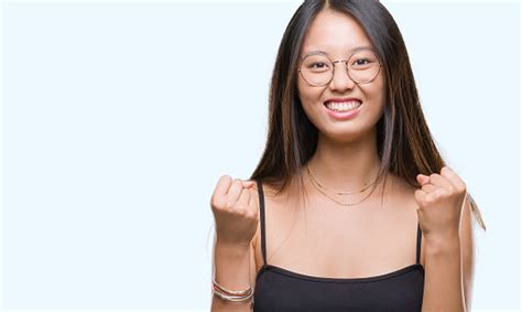 젊은 아시아 여자 매우 행복 하 고 흥분 무기와 우승자 제스처를 하 고 격리 된 배경 위에 안경을 쓰고 웃 고 성공을 위한 비명