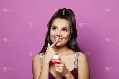 可爱的，有吸引力的，漂亮的，迷人的，惊讶的黑发的年轻微笑的女人时装模特抱着纸杯蛋糕在多彩的粉红色的背