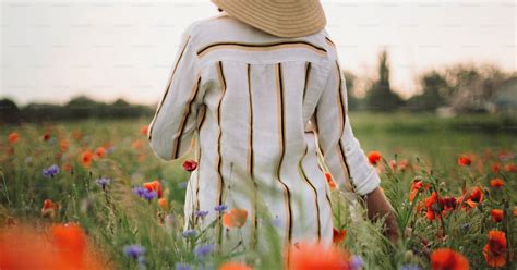 소박한 린넨 드레스를 입은 젊은 여성이 일몰 빛 아래 여름 초원 시골에서 양귀비와 수레국화 사이를 걷고 있다 시골의 느린 삶 단순한 삶을 즐기고 있습니다 야생화에