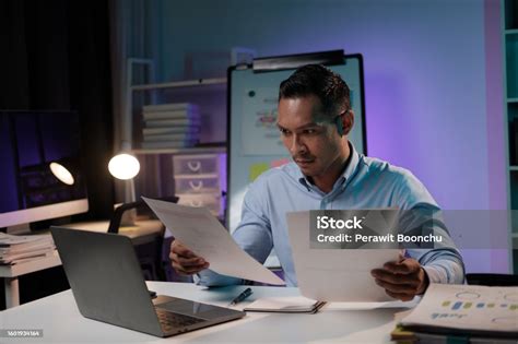 열심히 일하는 아시아 사업가는 자신의 프로젝트에 집중하고 손에 서류를 들고 사무실에서 혼자 밤에 초과 근무를합니다 Business Model Strategy에 대한 스톡