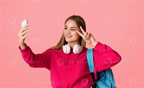 Smiling Teenage Girl With Backpack Makes Peace Sign With Hand And Takes
