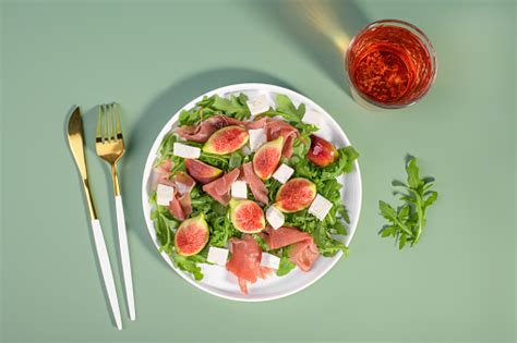 Arugula 죽은 태아 밝은 녹색 배경에 흰색 접시에 생 햄을 곁들인 가을 무화과 샐러드는 장미 와인과 함께 제공됩니다 가을에