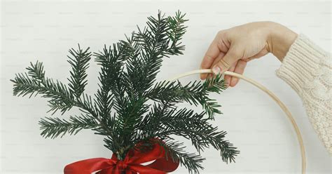 흰 벽 배경에 현대 크리스마스 화환을 들고 아늑한 스웨터를 입고 있다 메리 크리스마스와 해피 홀리데이 전나무 가지와 빨간