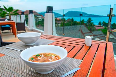 바다 쪽에 야외 테라스에서 식사 개념 나무 테이블과 빈티지 대나무 매트에 깊은 화이트 세라믹 수프 접시 0명에 대한 스톡 사진
