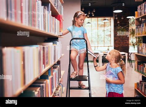 Two Schoolgirls Choosing Books In School Library Primary School