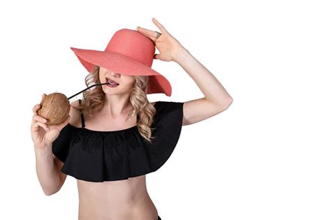흰색 배경에 고립 된 빨 대를 통해 코코넛에서 주스를 마시는 검은 수영복과 산호 모자를 입은 젊은 아름 다운 금발 여자의 초상화 감정에 대한 스톡 사진 및 기타 이미지