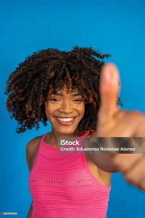 쾌활한 젊은 여성이 엄지 손가락을 치켜 세우고 승인과 긍정을 표현하는 신호를 보여줍니다 곱슬 머리에 대한 스톡 사진 및 기타 이미지 곱슬 머리 긍정적인 감정 표현
