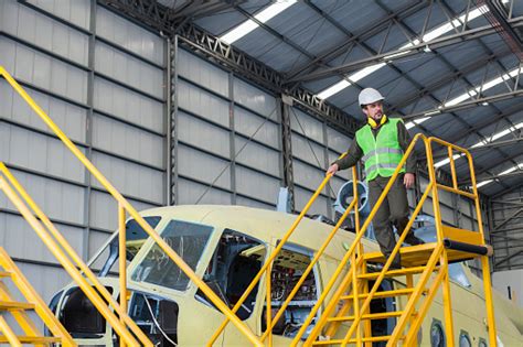 녹색 작업 바지 반사 조끼 흰색 헬멧과 안전 헤드폰을 입고 라틴 어 남자는 그가 위에서 비행기로 확인하는 데 사용하는 노란색