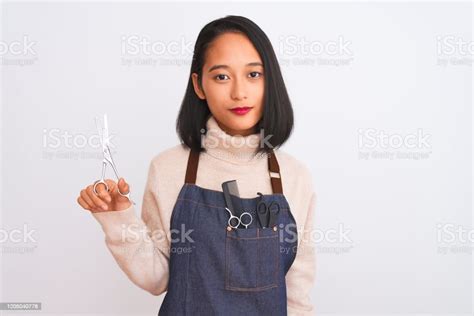 중국 미용사 여자 에이프런 을 입고 가위를 들고 고립 된 흰색 배경 에 자신감 표정으로 스마트 얼굴 생각 심각한 가위에 대한