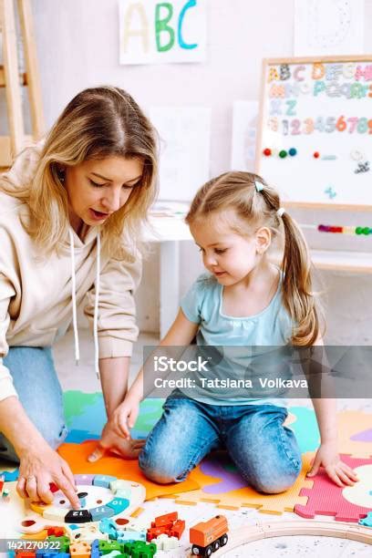 어린 소녀는 티셔츠를 입고 청바지는 젊은 여성 선생님과 함께 앉아 숫자로 시계의 일부를 가지고 노는 법을 가르칩니다 유치원에 대한 스톡 사진 및 기타 이미지 Istock