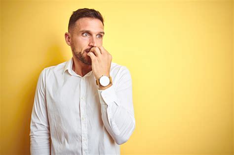 노란색 고립 된 배경 위에 우아한 흰색 셔츠를 입고 젊은 잘 생긴 남자는 손톱을 물고 입에 손을 긴장 찾고 불안 문제 남자에