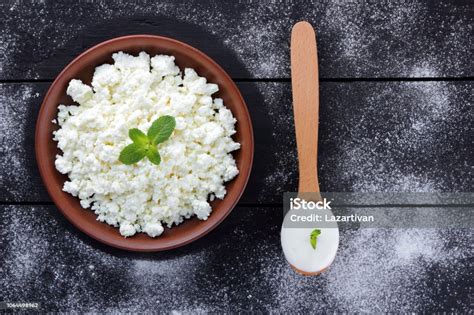나무판에 점토 그릇에 코 티 지 치즈입니다 나무로 되는 숟가락에 사 우 어 크림입니다 어두운 배경에 생활 용품입니다 신선한 박하