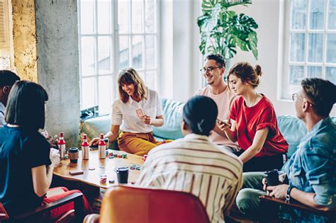 현대 아파트에서 알코올 음료와 포커 칩과 테이블에 앉아 보드 게임에서 재생 캐주얼 착용 다문화 사람들의 그룹 휴식을위한 친절한