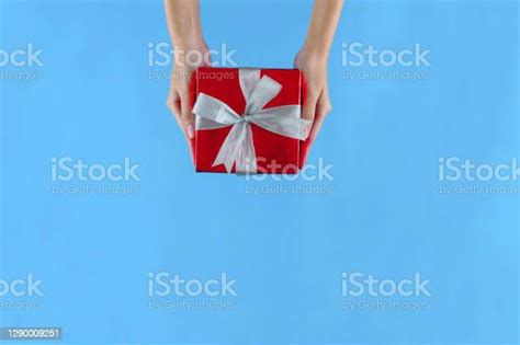 파란색 배경에 리본이 달린 빨간 종이에 싸여 있는 선물 상자를 들고 있는 여성의 손 맨 위 보기입니다 텍스트공간을 복사합니다 휴일 개념 기념일에 대한 스톡 사진 및 기타