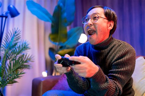 출구 쾌활한 아시아 일본 중반 성인 어둠 게임 컨트롤러에서 밤에 혼자 집에서 비디오 게임을하는 소파에 앉아있는 아시아 남성 반응 아시아 남성 반응은 게임 손에 자신의 승리를