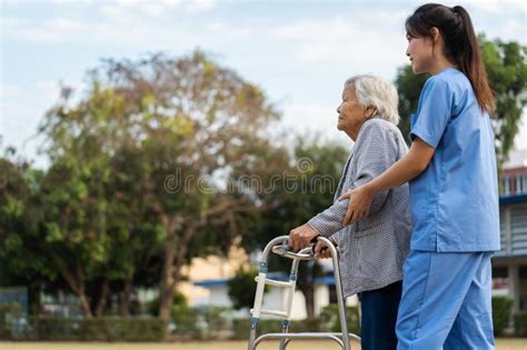 Caregiver Nurse Support Senior Woman Walking With Walker In Park Stock