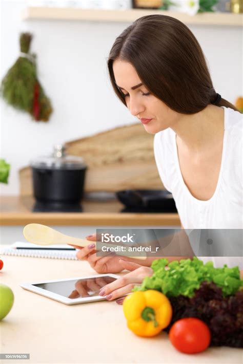 아름 다운 스페인 여자는 부엌에서 태블릿 컴퓨터를 사용 하는 동안 요리 저녁 이나 아침 식사에 대 한 새로운 레시피를 발견 하는 주부 가정 생활에 대한 스톡 사진 및 기타