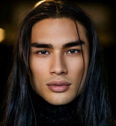 A Man With Long Black Hair Wearing A Turtle Neck Sweater And Looking At