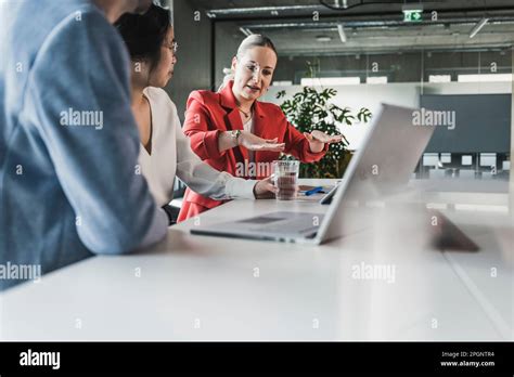 Businesswoman Explaining Colleagues Through Gestures At Office Stock