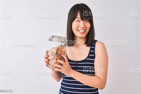 행복한 얼굴 서서 치아를 보여주는 자신감 미소와 함께 미소와 고립 된 흰색 배경 위에 쿠키의 항아리를 들고 젊은 아름다운 중국