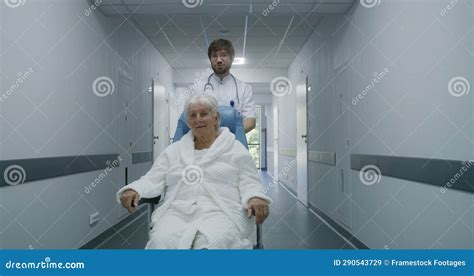Young Doctor Transports Senior Female Patient In Wheelchair Stock Image