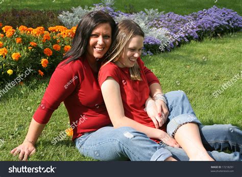 Beautiful Barefoot Mother And Daughter Sitting On The Grass With Flowers In The Background Stock