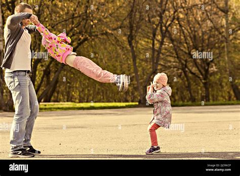 Dad Plays With His Daughters In The Park Twirling A Girl Around
