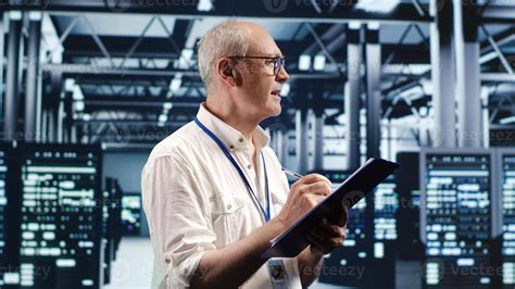 Elderly Engineer Looking Around High Tech Data Center Using Clipboard
