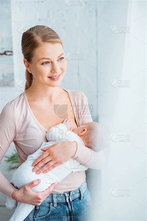 快乐的年轻妇女母乳喂养婴儿和看别处而站在家里素材 花瓣网