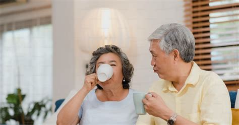 아시아 노부부는 따뜻한 커피를 마시고 집 거실에서 함께 이야기를 나누고 부부는 집에서 휴식을 취할 때 소파에 누워 사랑의