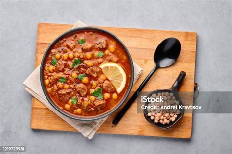 회색 콘크리트 테이블 상단에 검은 그릇에 모로코 하리라 수프 하리라는 양고기 또는 쇠고기 고기 병아리콩 렌즈콩 토마토 실리언트로모로코 요리 요리입니다 라마단 이프타르 음식