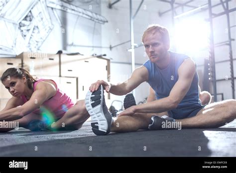 Confident Man And Woman Doing Stretching Exercise In Crossfit Gym Stock