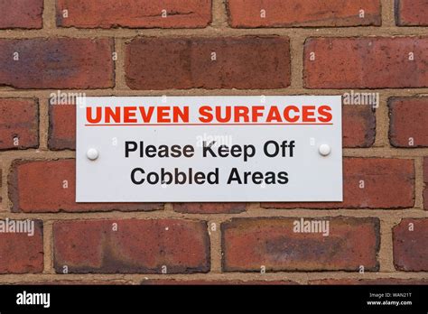 Sign Saying Uneven Surfaces Please Keep Off Cobbled Areas Fixed To Brick Wall Stock Photo Alamy