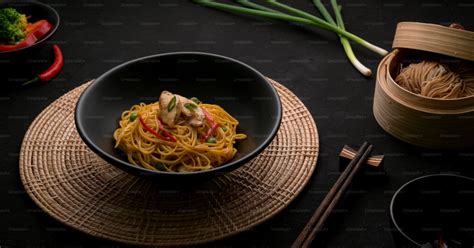 Schezwan 국수 또는 Chow Mein의 크롭 샷과 야채 닭고기 칠리 소스가 검은 그릇에 담겨 제공되며 검은 테이블에 재료 사진 Unsplash의 식당 배경 이미지